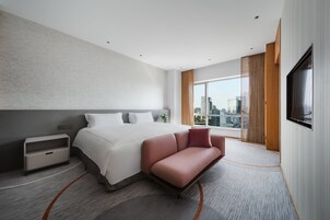 Quarto de hotel moderno com uma cama grande, um sofá, uma TV e vista para a cidade.