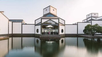 Um edifício moderno com entrada de vidro central, rodeado por um espelho d'água.