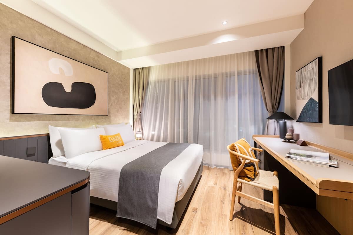 Quarto de hotel moderno com uma cama bem arrumada, uma mesa de trabalho e uma cadeira.