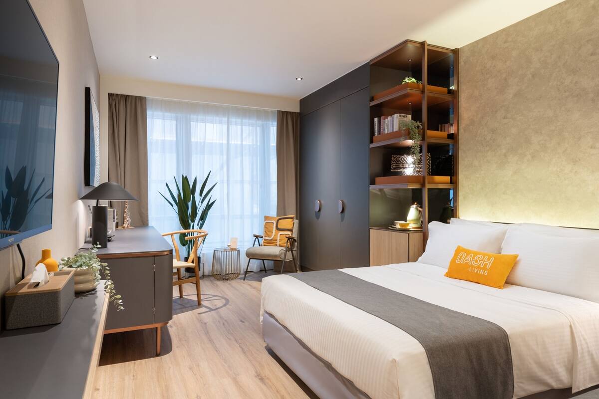 Quarto de hotel moderno com uma cama grande, uma escrivaninha, uma estante de livros e uma televisão.