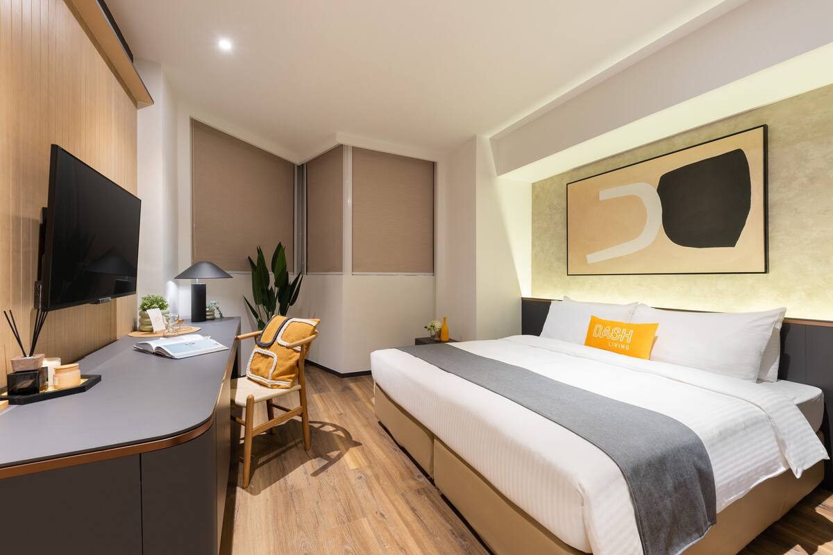 Quarto de hotel moderno com uma cama grande, uma mesa de escritório, uma cadeira, uma televisão e uma obra de arte na parede.