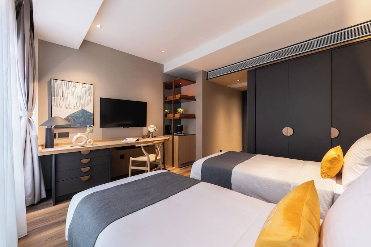 Quarto de hotel moderno com duas camas, uma escrivaninha, televisão e um guarda-roupa.
