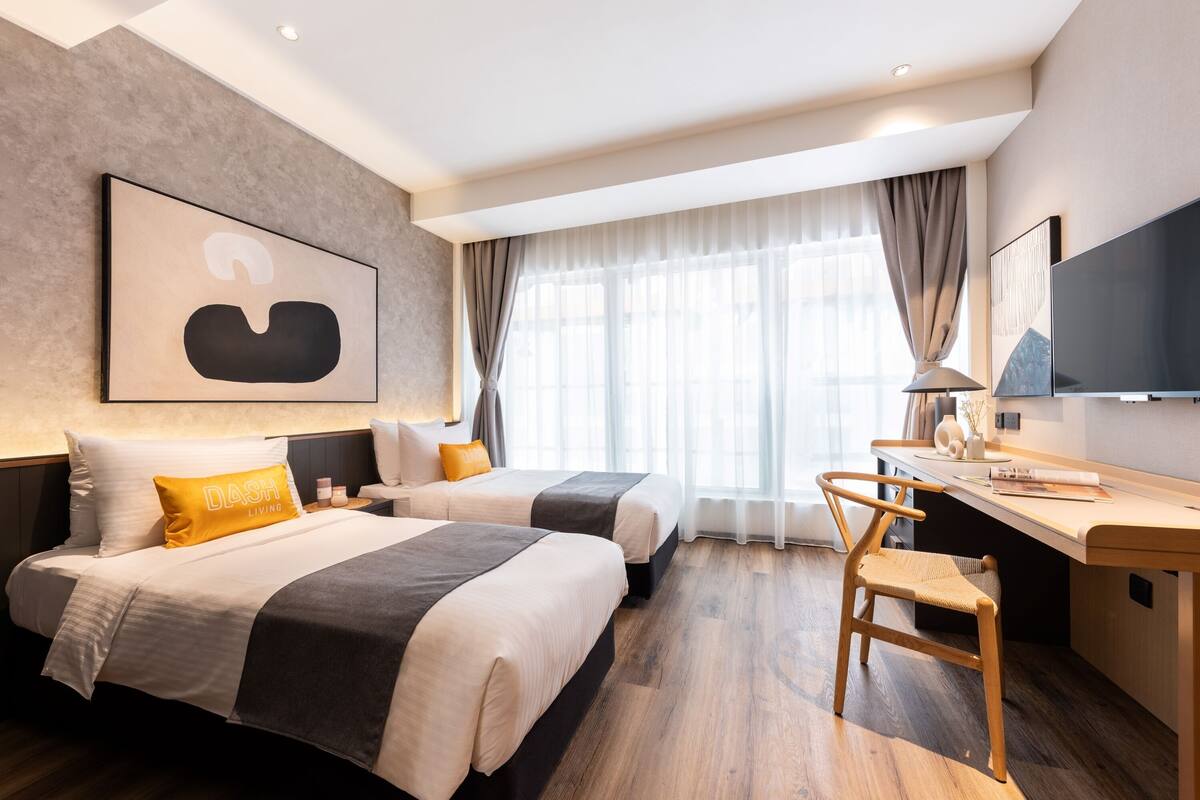 Quarto de hotel moderno com duas camas, uma escrivaninha e uma televisão grande.