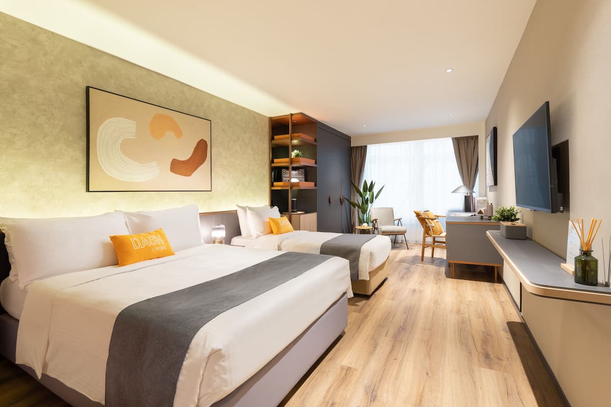 Quarto de hotel moderno com duas camas, uma escrivaninha, uma cadeira, uma televisão e uma estante de livros.
