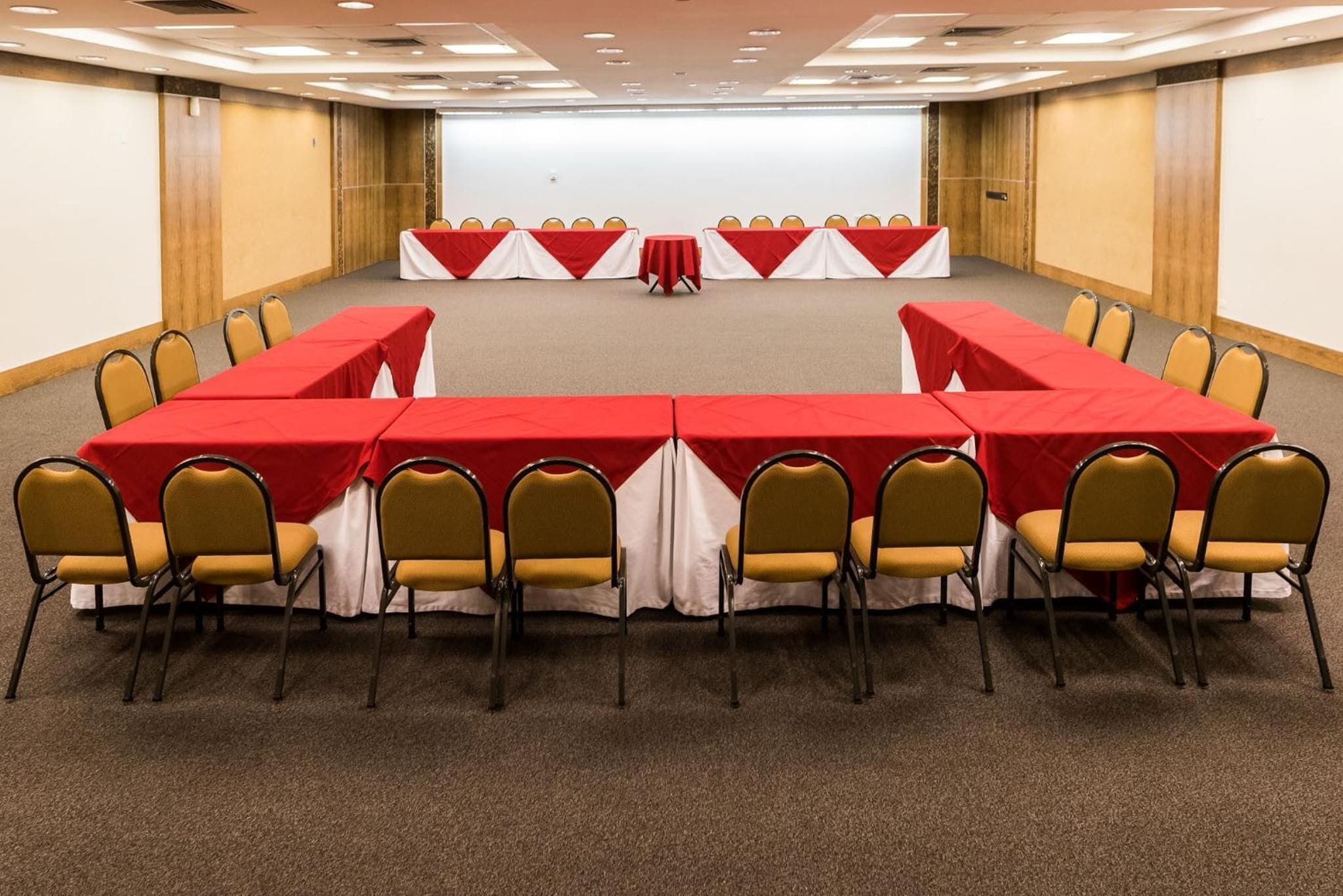 Uma sala de conferências com uma mesa comprida coberta por um tecido vermelho, rodeada por cadeiras amarelas.
