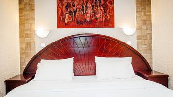 Uma cama com cabeceira de madeira, duas almofadas brancas e um quadro abstrato vermelho acima.