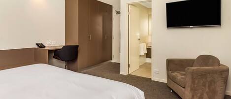 Quarto de hotel com uma cama, escrivaninha, cadeira, guarda-roupa e televisão.