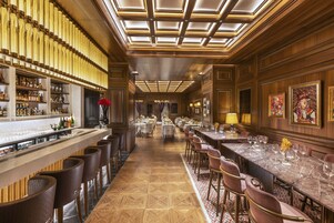 Uma área de bar com um balcão extenso, diversos taburetes e uma variedade de garrafas e copos.