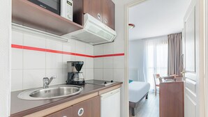 Uma cozinha compacta com pia, cafeteira e micro-ondas.