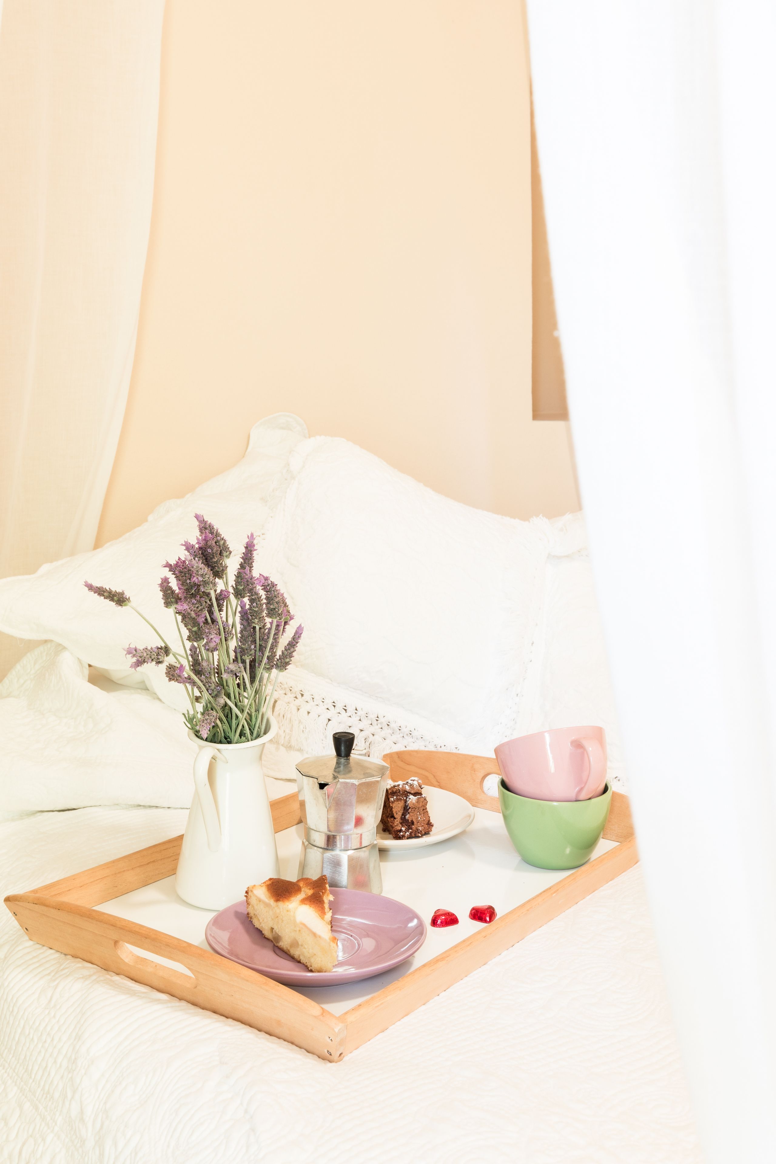 Uma bandeja com uma fatia de bolo, uma xícara, um vaso de flores e um bule na cama.