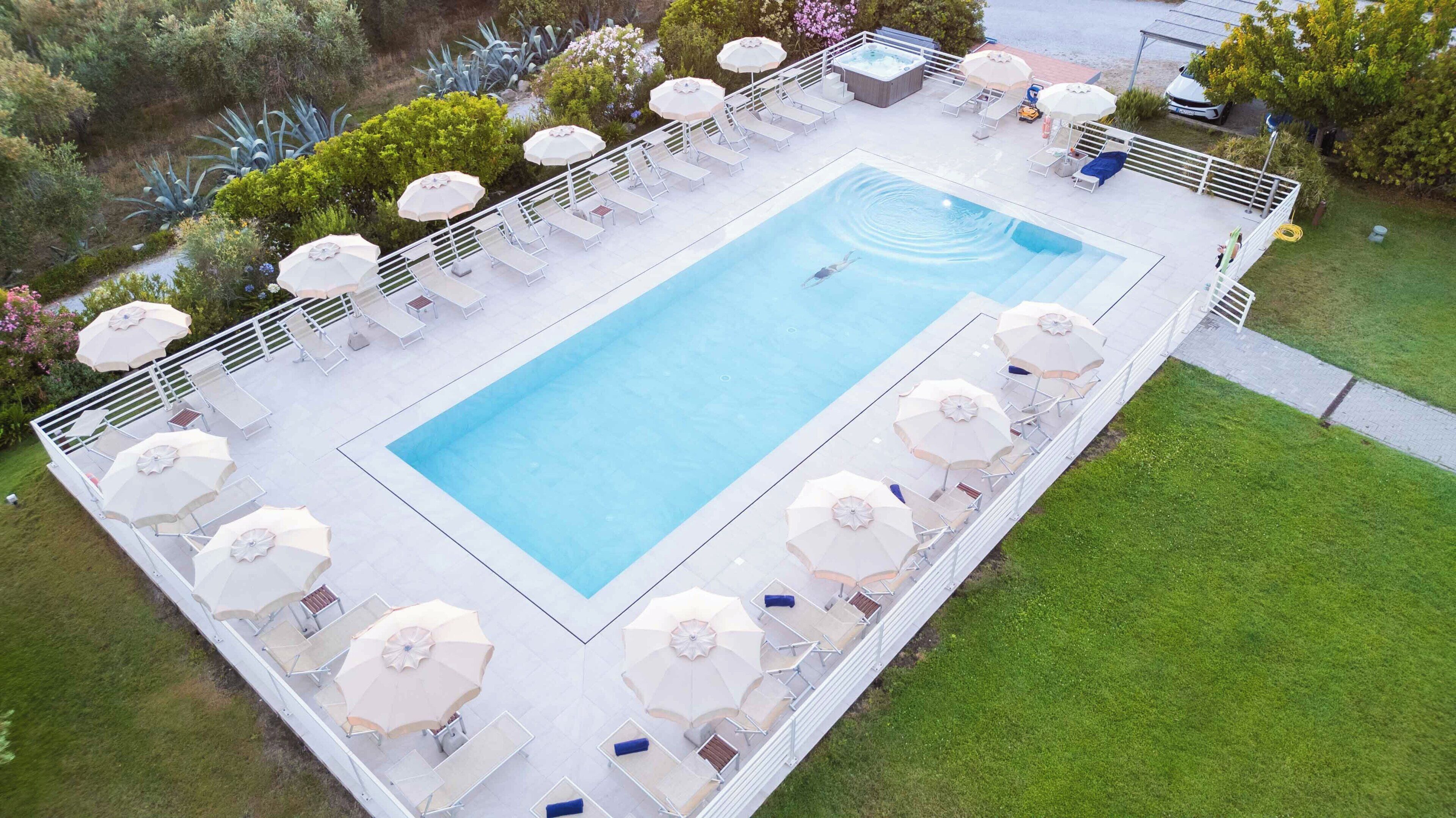 Piscina retangular com cadeiras de praia e guarda-sóis ao redor.