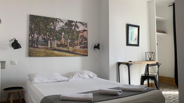 Quarto de hotel com cama, escrivaninha e uma cadeira. Há um quadro na parede e uma moldura acima da escrivaninha.