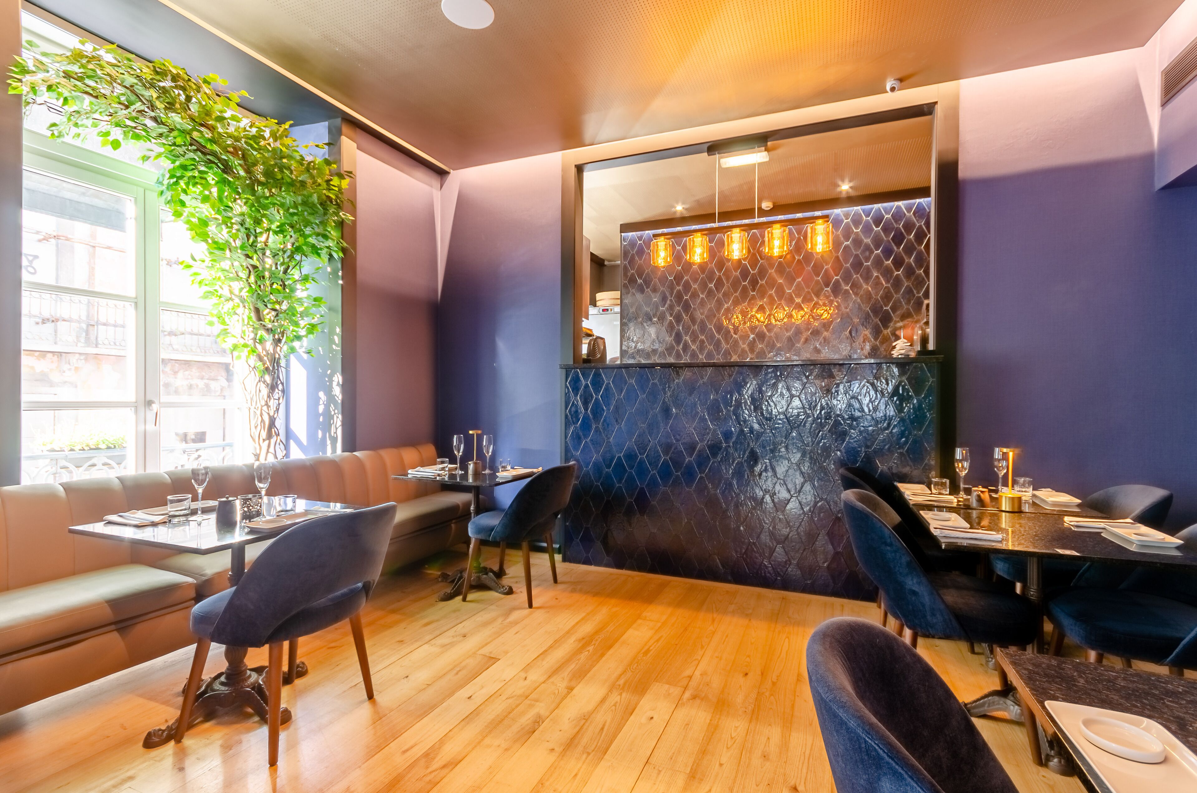 Um restaurante com soalho de madeira, cadeiras estofadas em azul e uma área de estar com um banco acolchoado.