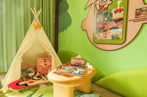 Espaço infantil com um tipi, uma mesa de brinquedos e uma parede com um personagem de desenho animado.