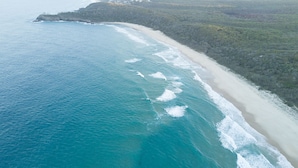 Vista aérea de uma área costeira com praia de areia e floresta densa.