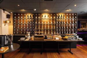 Uma área de bar com uma parede de garrafas de vinho, uma máquina de café e diversos alimentos no balcão.