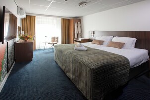 Quarto de hotel com cama grande, escrivaninha, cadeira e guarda-roupa.