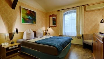 Quarto de hotel com cama, mesa de cabeceira, abajur, cadeira e janela com cortinas.