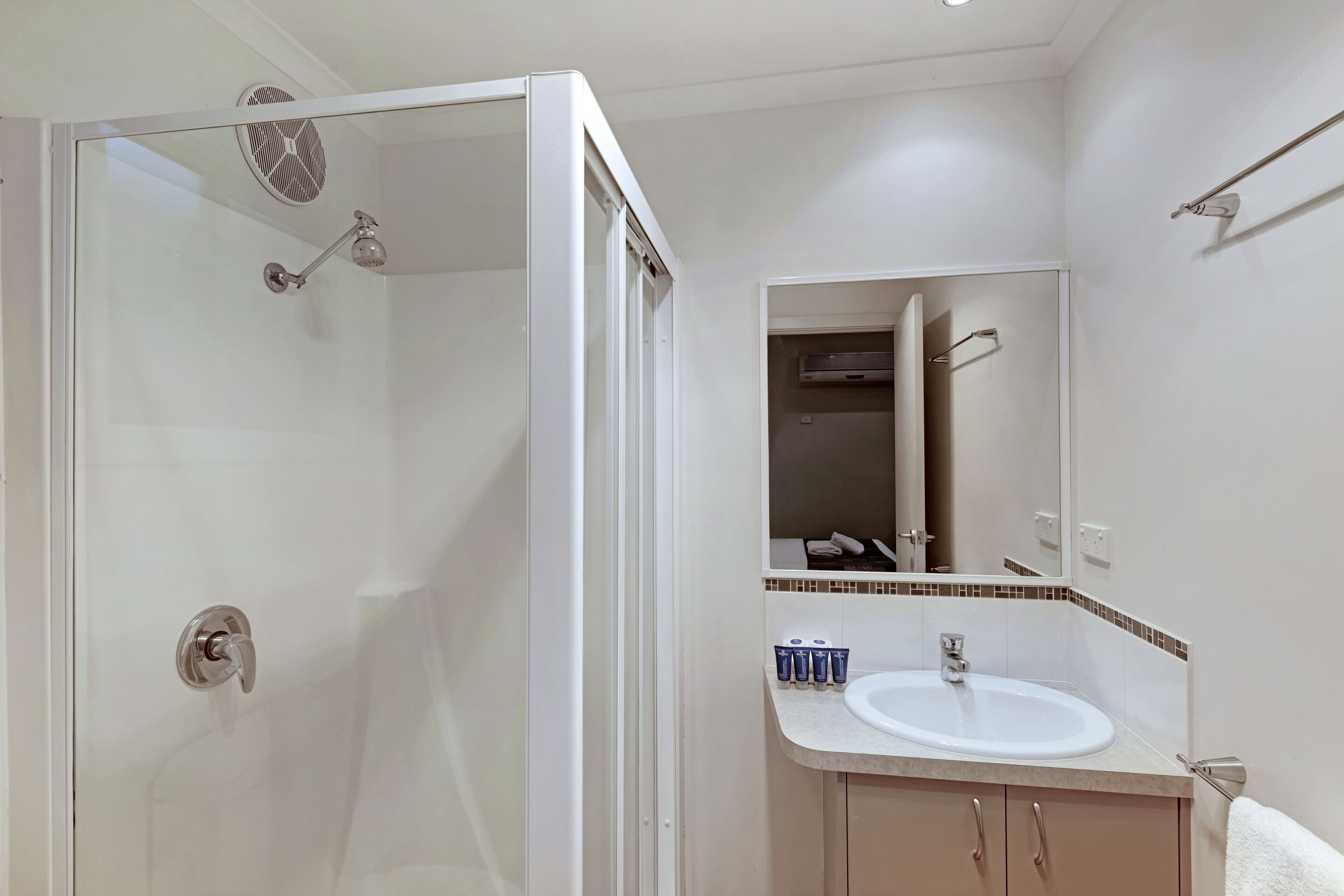 Uma casa de banho moderna com cabine de duche em vidro, lavatório com espelho e um porta-toalhas.