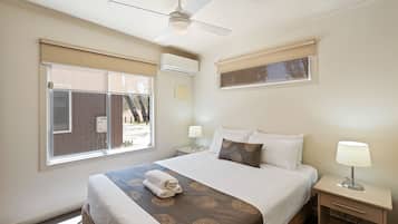 Quarto de hotel com cama, mesa de cabeceira, luminária, ar condicionado, ventilador de teto e janela com persianas.
