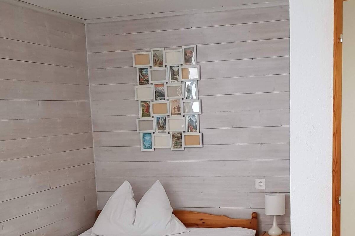 Quarto com cama de madeira, mesa de cabeceira com abajur e parede decorada com quadros.