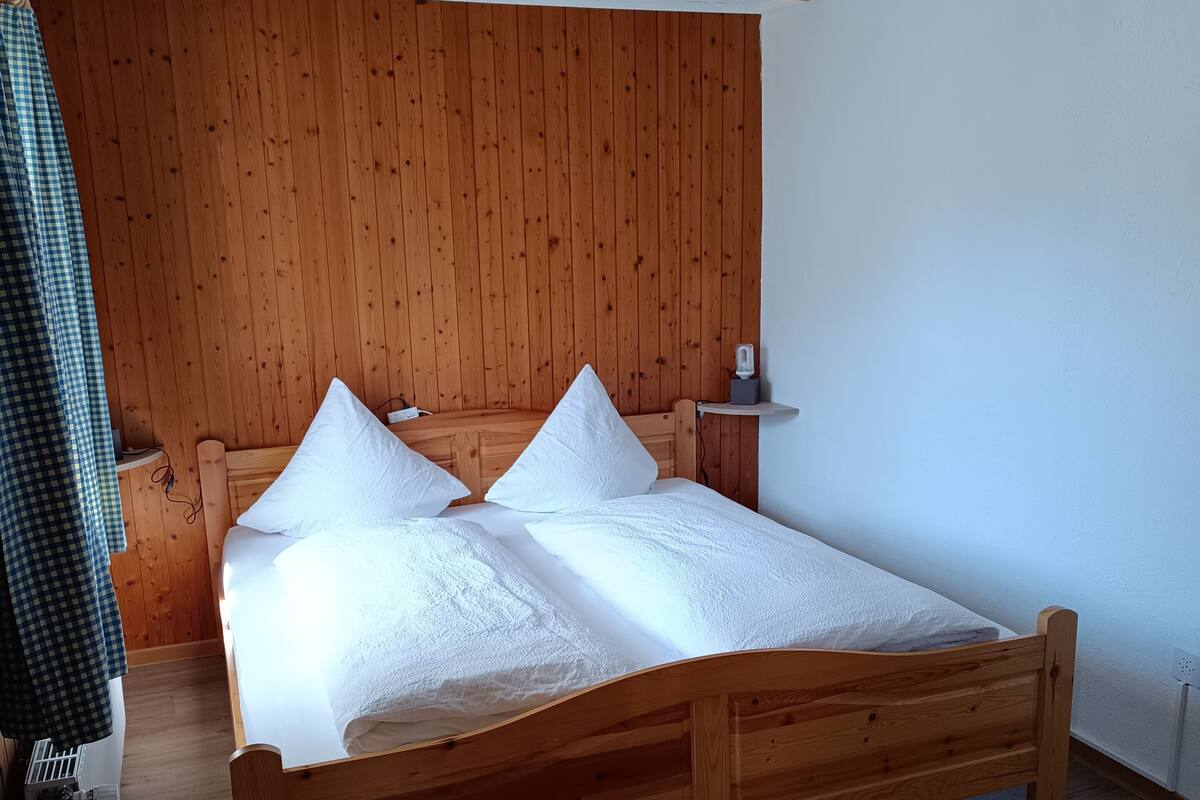 Uma cama de madeira com cabeceira, roupa de cama branca e uma mesa de cabeceira com abajur.