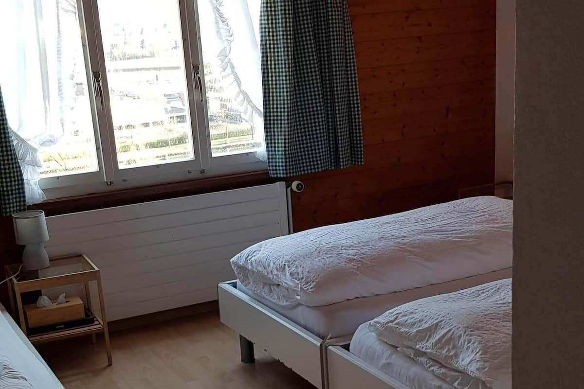 Quarto com cama grande, mesa de cabeceira, abajur e janela com cortinas.