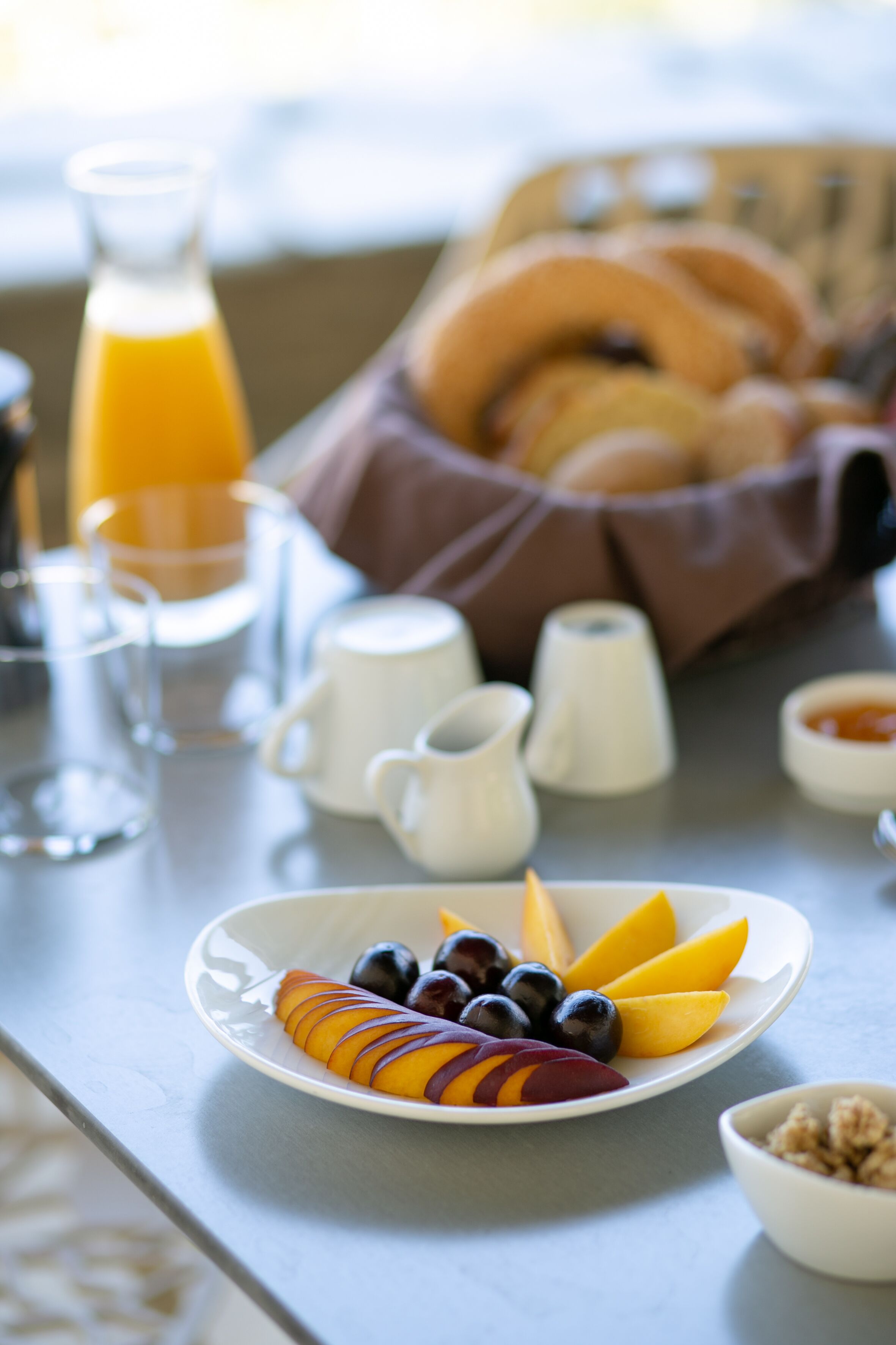 Uma mesa de café da manhã com uma travessa de frutas, um copo de suco de laranja e uma cesta de doces.