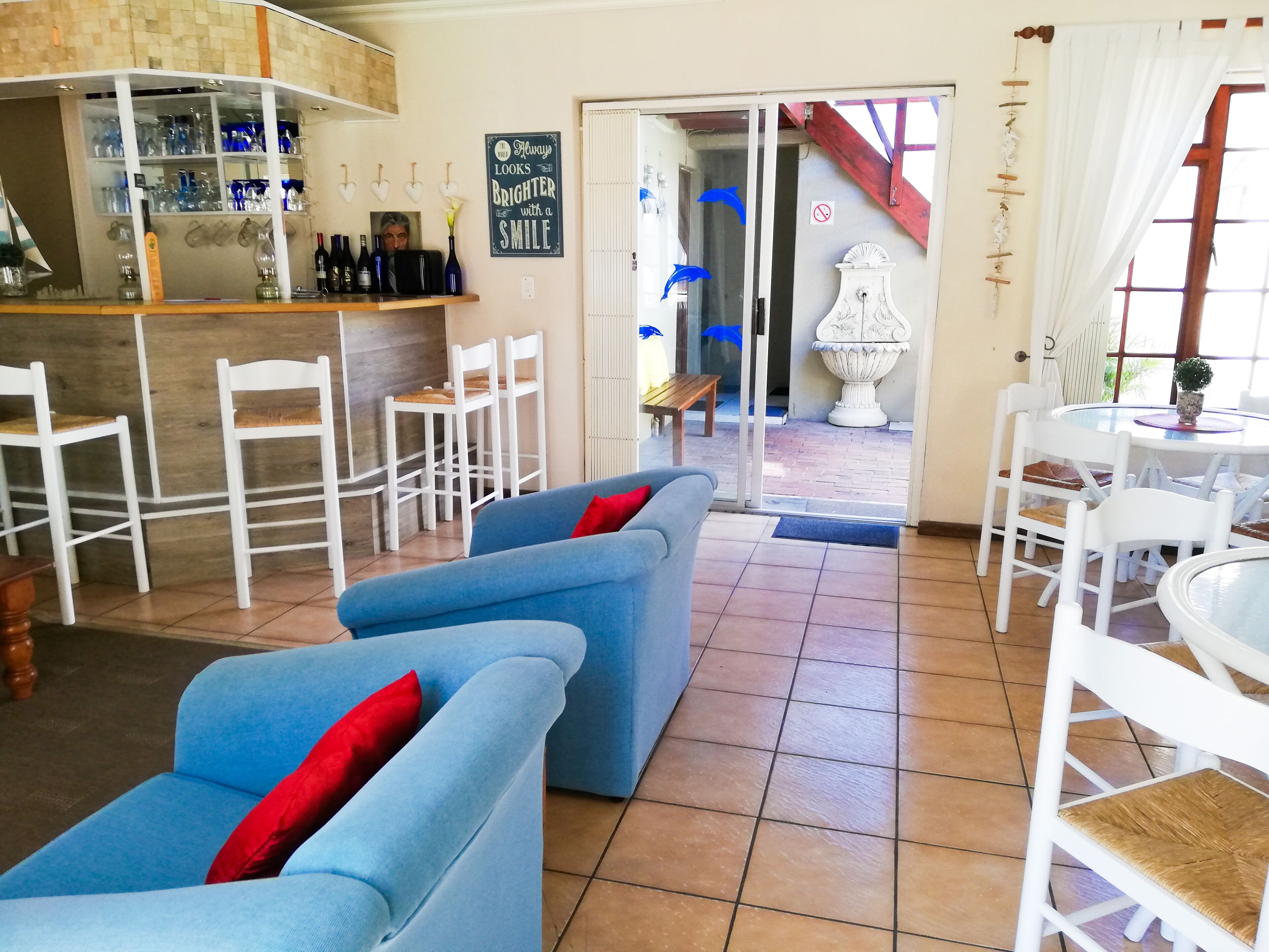 Um interior aconchegante com sofás azuis, área de bar, cadeiras brancas e um letreiro decorativo na parede.
