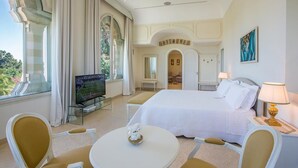 Quarto de hotel com uma cama grande, televisão, área de refeições e vista para o exterior.