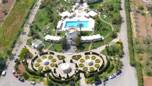 Vista aérea de um resort com piscina central, várias villas e jardins bem cuidados.