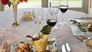 Uma mesa de jantar posta com comida, copos de vinho e talheres.