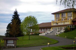 Um hotel com uma placa que diz “Domaine de Revernmont”. Apresenta um edifício de vários andares com telhado inclinado, uma escadaria que leva à entrada e um gramado bem cuidado.