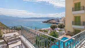 Uma varanda com vista para o mar e montanhas, piscina e um prédio com persianas verdes.
