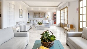 Ampla sala de estar com sofá, mesa de centro com planta e cozinha ao fundo.