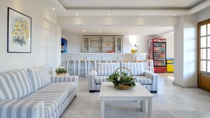 Uma sala de estar moderna com sofás listrados, uma mesa de centro branca e uma área de cozinha ao fundo.