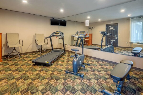 Sala de ginástica com esteiras, elíptica e banco.