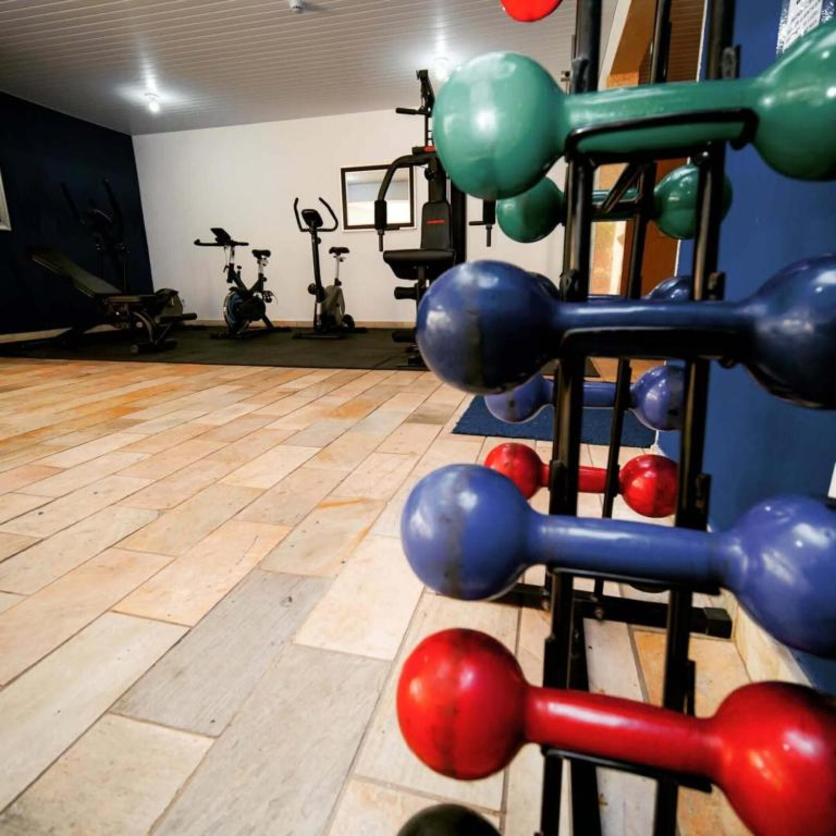 Uma academia com equipamentos de exercício, incluindo halteres e uma bicicleta ergométrica.
