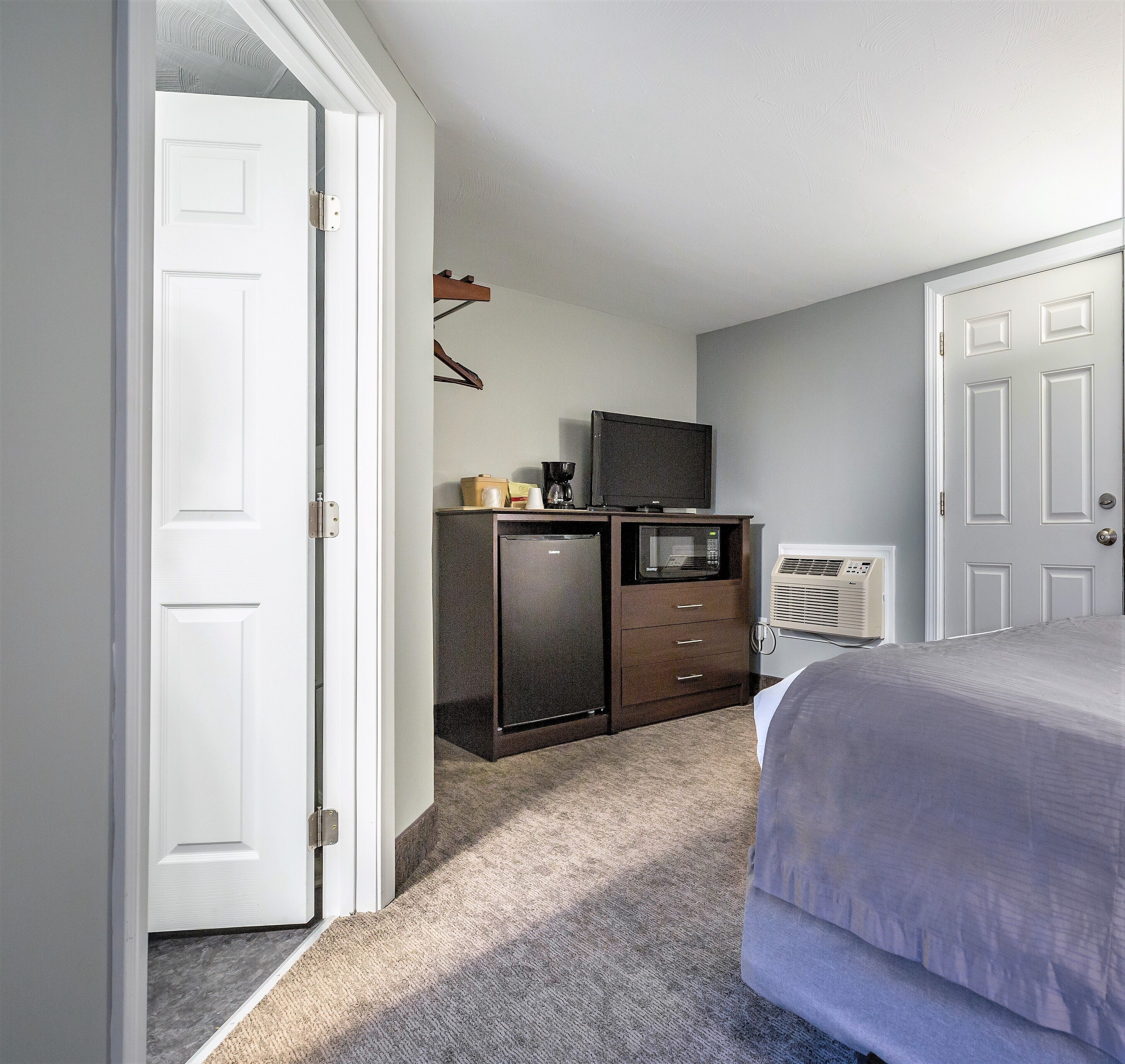 Quarto com cama, cômoda, micro-ondas e porta.