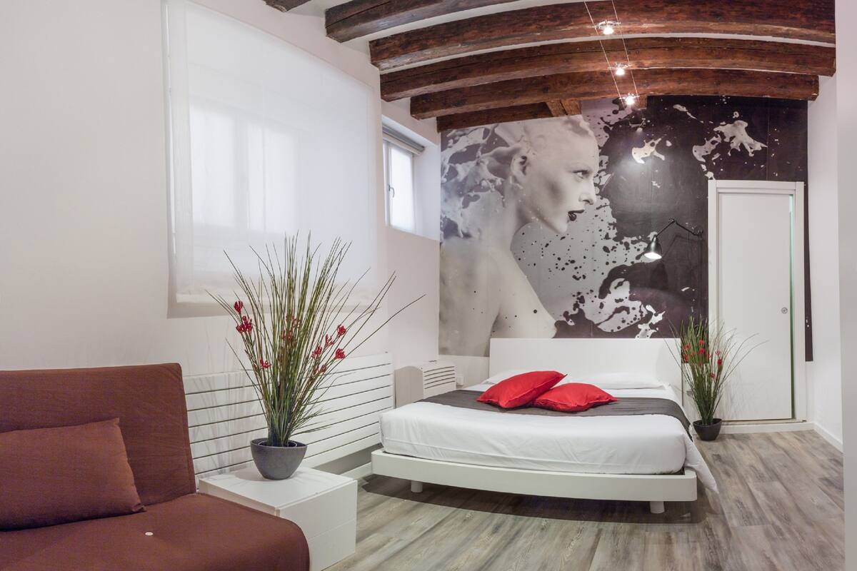 Quarto moderno com cama branca, almofadas vermelhas e um quadro abstrato grande na parede.