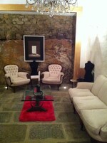 Uma sala de estar com duas poltronas, um sofá, uma mesa de centro de vidro e uma parede de pedra.