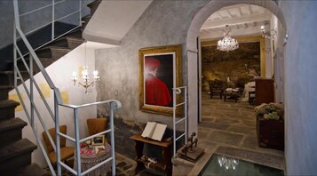 Uma escadaria com corrimão de metal, um quadro emoldurado na parede, um candelabro e piso de pedra.