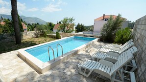 Piscina com escadas, piso de pedra e cadeiras de lounge brancas.