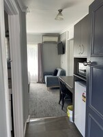 Um espaço compacto com cozinha americana, um sofá cinza, uma pequena mesa de jantar e um ventilador de teto.