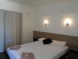Quarto de hotel com uma cama, duas luzes fixadas na parede, uma cortina e uma mesa de cabeceira.