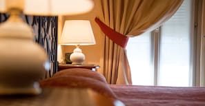 Quarto de hotel com cama, luminária de cabeceira e janela com cortinas.
