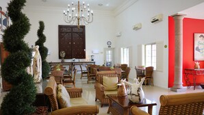Um hall amplo com móveis de vime, um lustre grande e uma parede de destaque vermelha.
