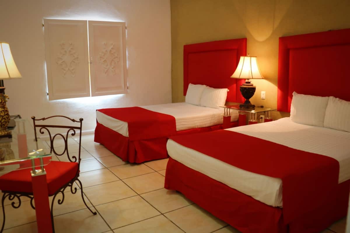 Quarto de hotel com duas camas, uma mesinha, uma cadeira e janela com vista.