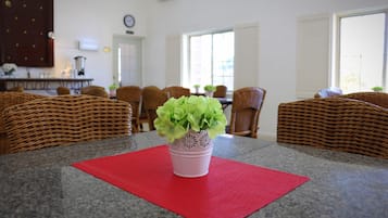 Uma área de refeições com cadeiras de vime, um jogo de mesa vermelho e uma planta em vaso sobre uma mesa de granito.