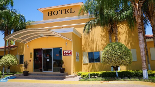 Um hotel com fachada amarela, um letreiro 'HOTEL' acima da entrada e uma placa 'Zar Hoteles'.